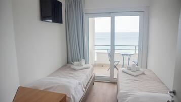 Quarto de hotel com duas camas, uma secretária de madeira, televisão e varanda com mesa e cadeiras.