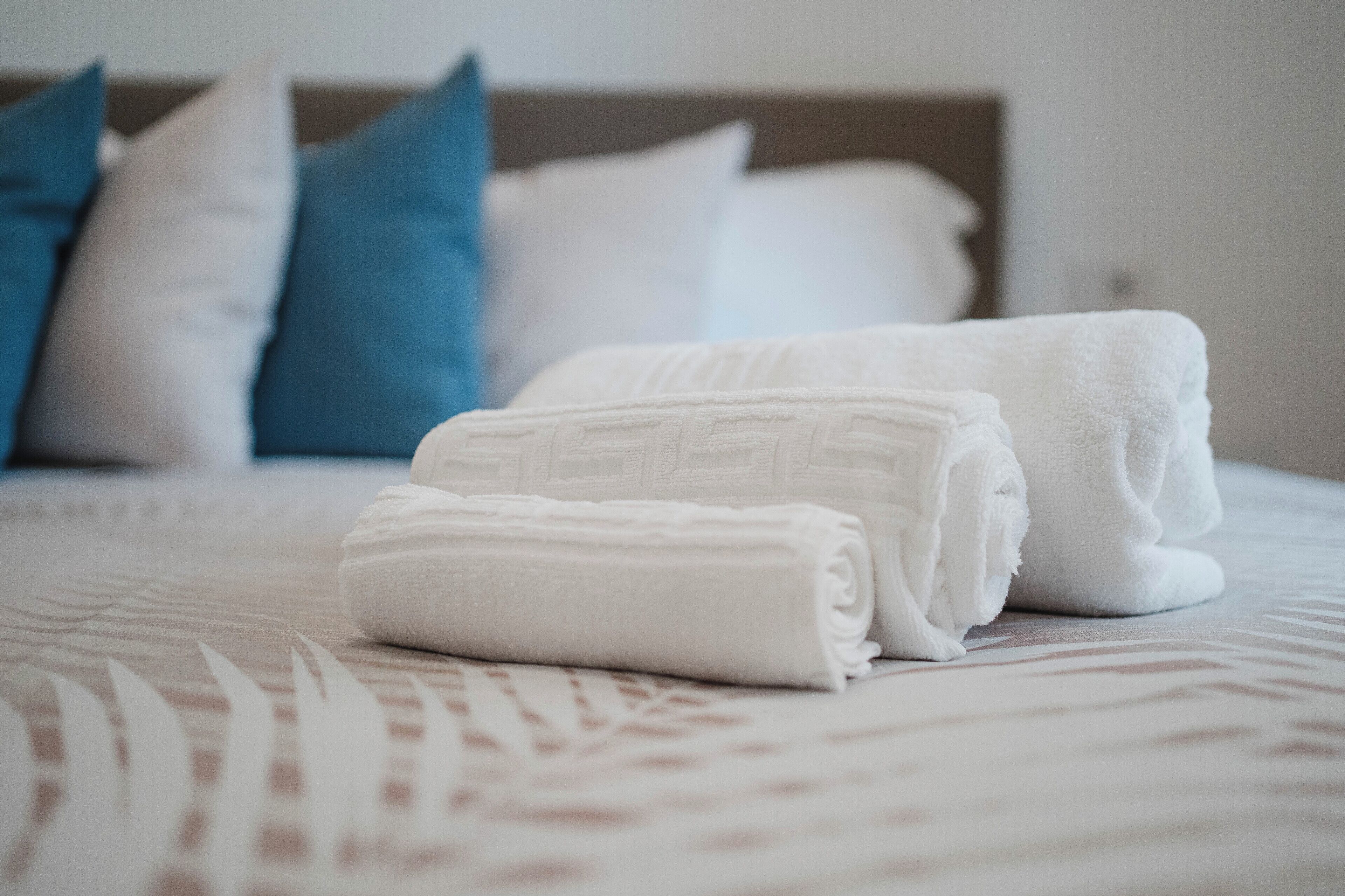Cama bem arrumada com almofadas brancas e azuis, uma toalha branca enrolada e um cobertor branco.