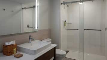 Um banheiro moderno com um espelho grande, pia branca, chuveiro com porta de vidro e vaso sanitário.