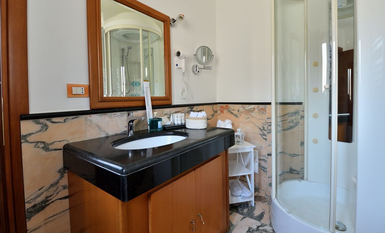 Casa de banho com toucador em mármore, cabine de duche com vidro e secador de cabelo fixo.
