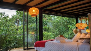 Quarto com uma janela grande, uma cama com manta vermelha e um candeeiro suspenso.