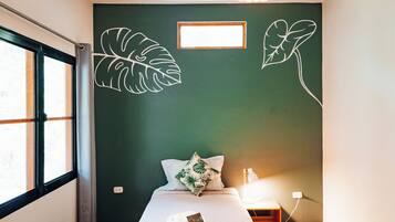 Quarto com cama, mesa de cabeceira, luminária, janela e decoração na parede.