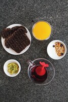 Uma mesa de pequeno-almoço sobre uma bancada de granito, com torradas, sumo de laranja, granola, iogurte e uma chávena de café.