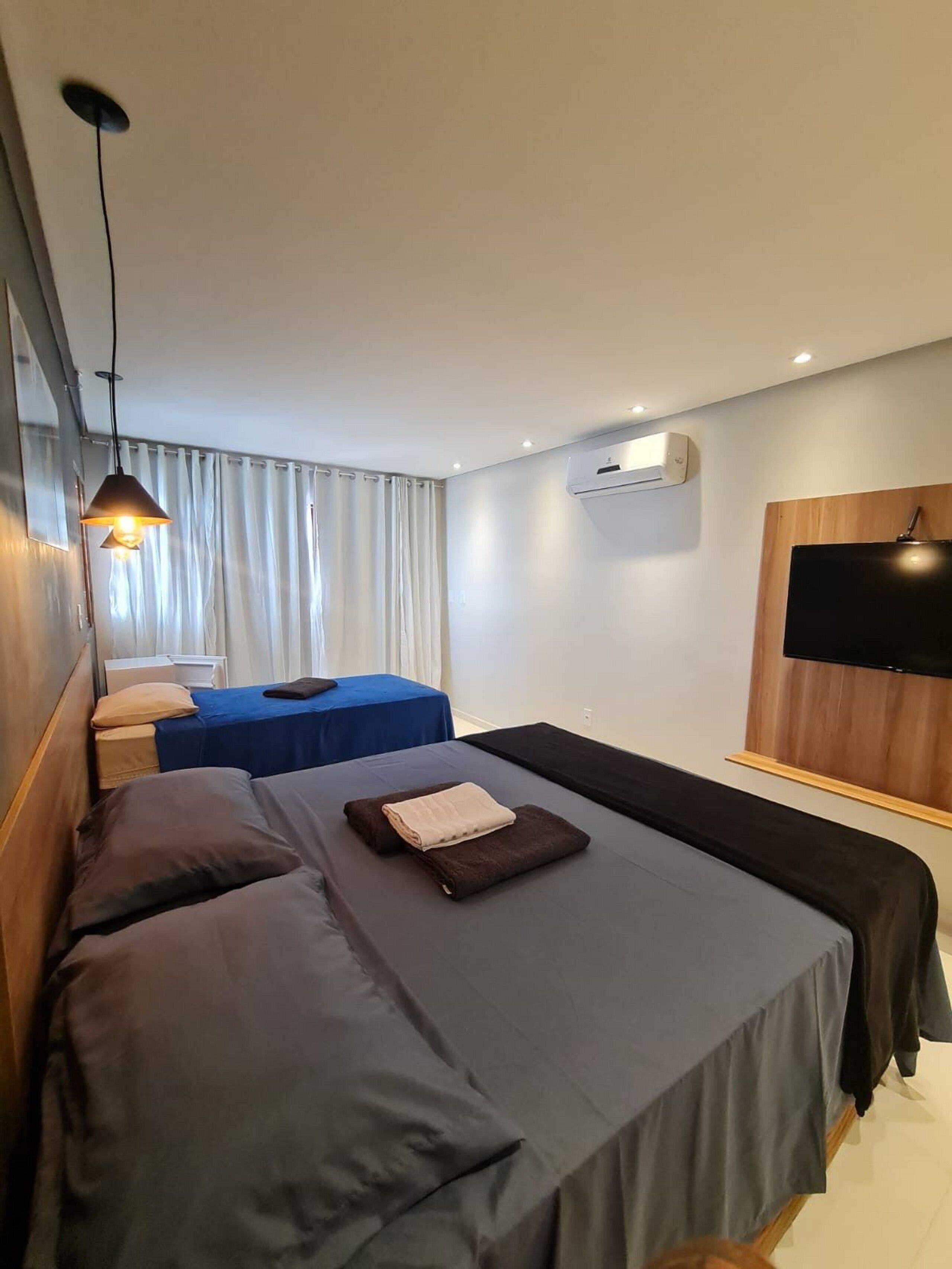 Quarto de hotel com duas camas, uma TV, ar condicionado e uma luminária de teto.