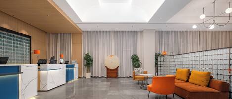 Um lobby moderno de hotel com balcão de recepção, área de estar e uma grande janela.
