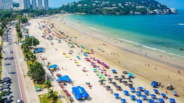 Uma praia com fileiras de guarda-sóis e pessoas.