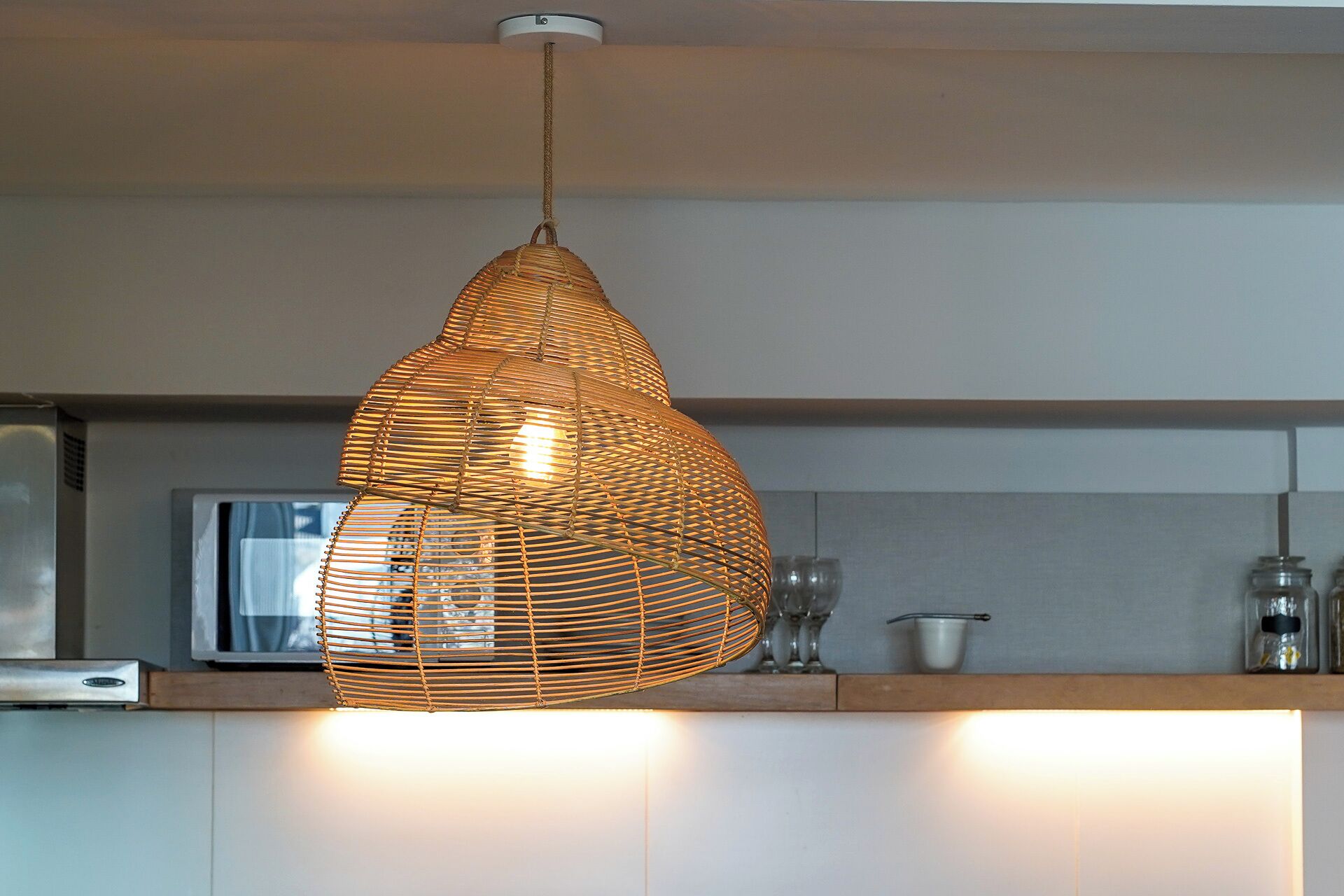 Uma cozinha com luminária trançada pendente, eletrodomésticos de aço inoxidável e bancada de madeira.