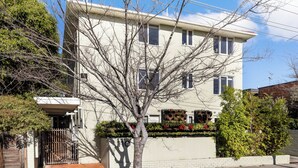Uma casa de dois andares com varanda frontal, garagem e um pequeno jardim com diversas plantas e flores.