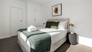 Quarto bem arrumado com cama, abajur e uma obra de arte emoldurada na parede.