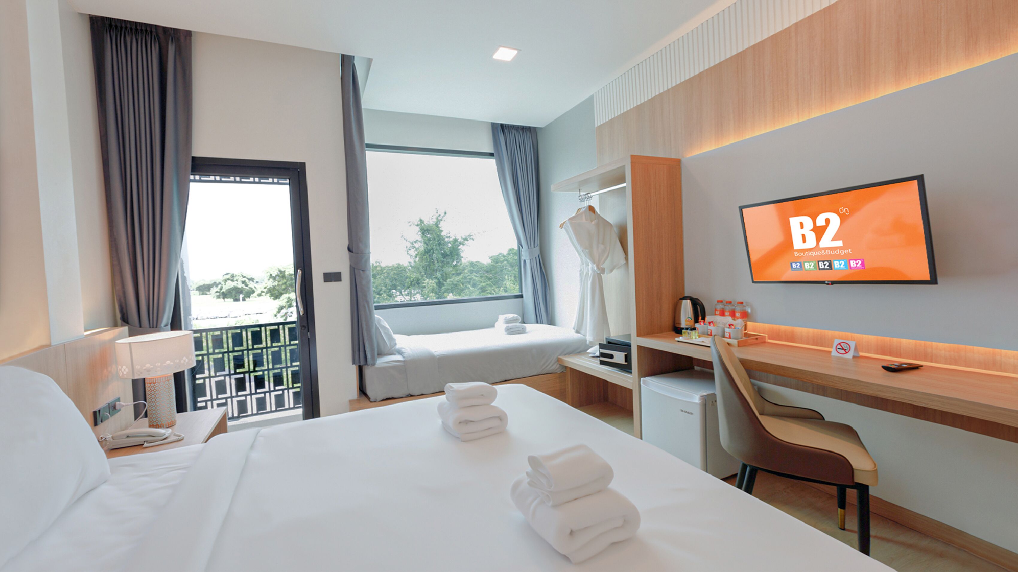 Quarto de hotel com cama, escrivaninha, cadeira, televisão e janela com cortinas.