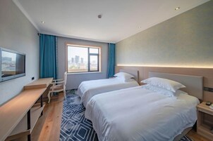 Quarto de hotel com duas camas, uma escrivaninha, uma cadeira, uma televisão e uma janela com cortinas.