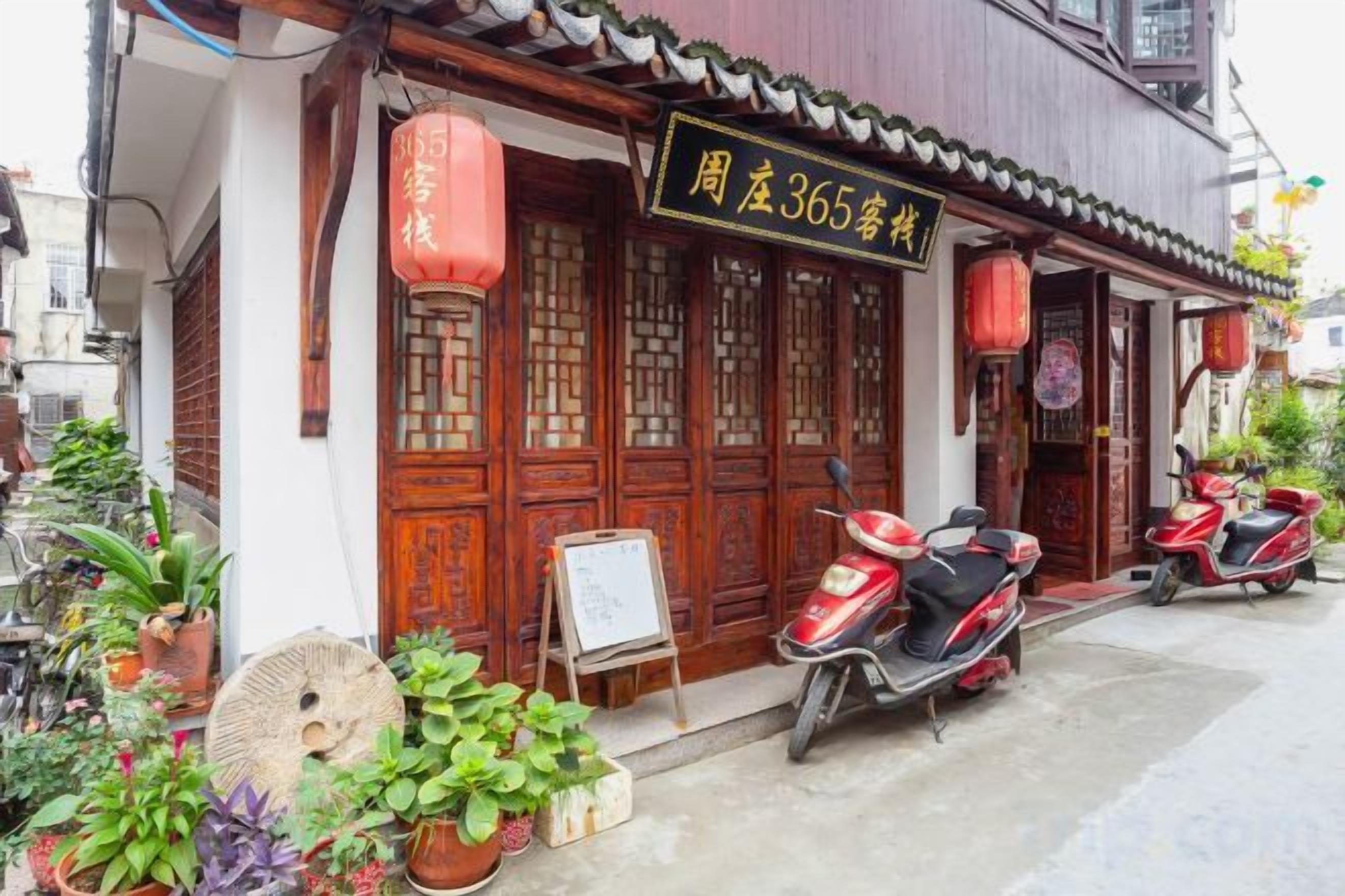 Edifício tradicional com placa, plantas em vasos e scooters estacionadas na frente.
