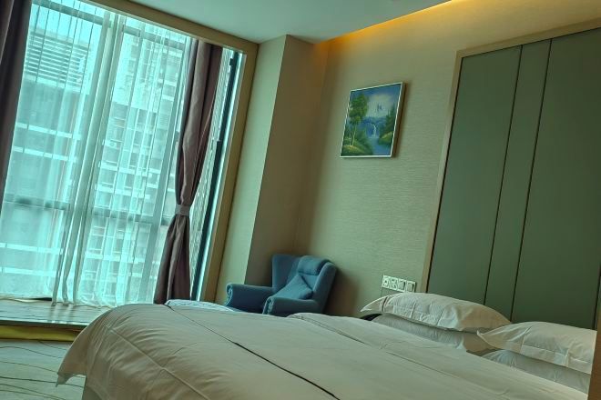 Quarto de hotel com cama, uma cadeira, janela com cortinas e um quadro na parede.