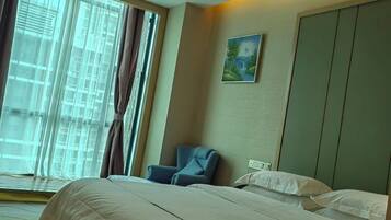 Quarto de hotel com cama, uma cadeira, janela com cortinas e um quadro na parede.