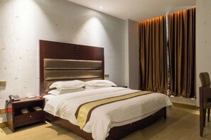 Quarto de hotel com uma cama grande, mesa de cabeceira com telefone e janela com cortinas.