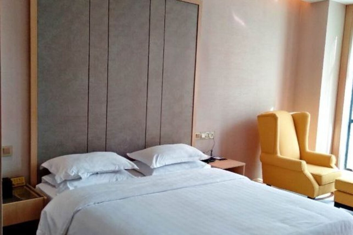 Quarto de hotel com cama, mesa de cabeceira, cadeira e uma janela grande.