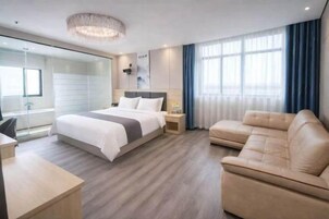 Quarto de hotel moderno com cama, escrivaninha, sofá e um espelho grande.