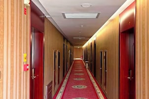 Corredor de hotel com portas em ambos os lados, tapete vermelho e teto com iluminação embutida.