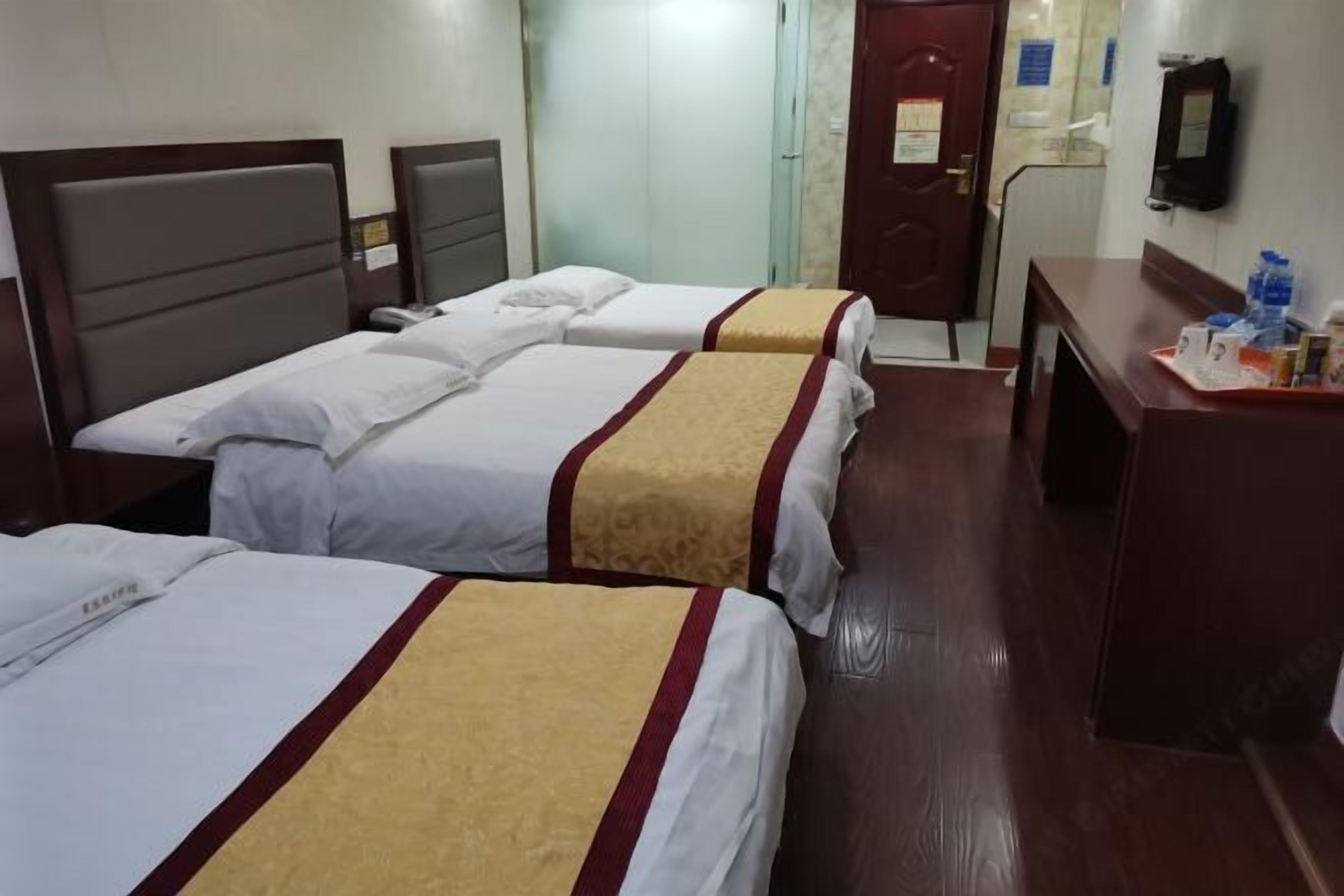 Quarto de hotel com três camas, uma mesa e uma porta.