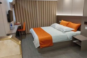 Quarto de hotel com cama, escrivaninha, cadeira e televisão.