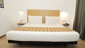 Quarto de hotel com uma cama grande, duas mesas de cabeceira, uma cabeceira de madeira e um edredom estampado.
