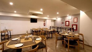Uma sala de jantar com várias mesas e cadeiras, um extintor de incêndio na parede e quadros decorativos.