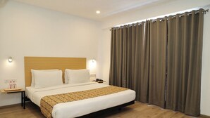 Quarto de hotel com cama, mesas de cabeceira, telefone e cortinas.