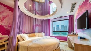 Quarto moderno com design de teto circular, uma cama grande, uma escrivaninha e vista para a cidade.