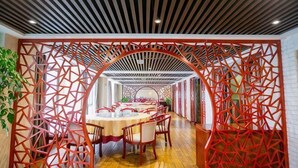 Uma área de refeições com mesas e cadeiras redondas, um separador geométrico vermelho e um teto com padrão listrado.