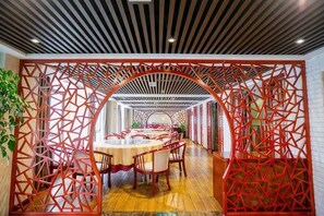 Uma área de refeições com mesas e cadeiras redondas, um separador geométrico vermelho e um teto com padrão listrado.