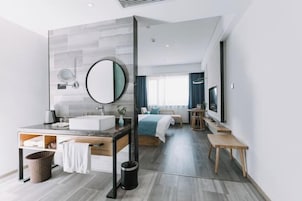 Quarto de hotel moderno com um espelho grande, pia, mesa de cabeceira, cama, televisão e janela com cortinas.