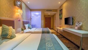 Quarto de hotel com duas camas, televisão, escrivaninha e uma pequena mesa com uma planta.