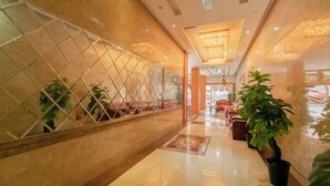 Um hall de hotel com um corredor comprido, chão de azulejos e plantas em vasos.