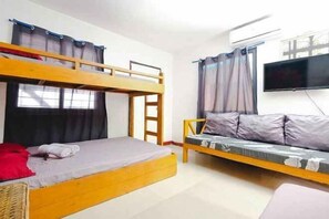 Quarto com cama de solteiro, sofá, televisão e janela com cortinas.