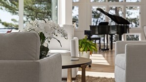 Uma sala de estar moderna com um piano, cadeiras brancas e um vaso de orquídeas brancas.