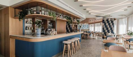 Uma área de bar moderna com balcão curvo, banquetas e diversos frascos e plantas.