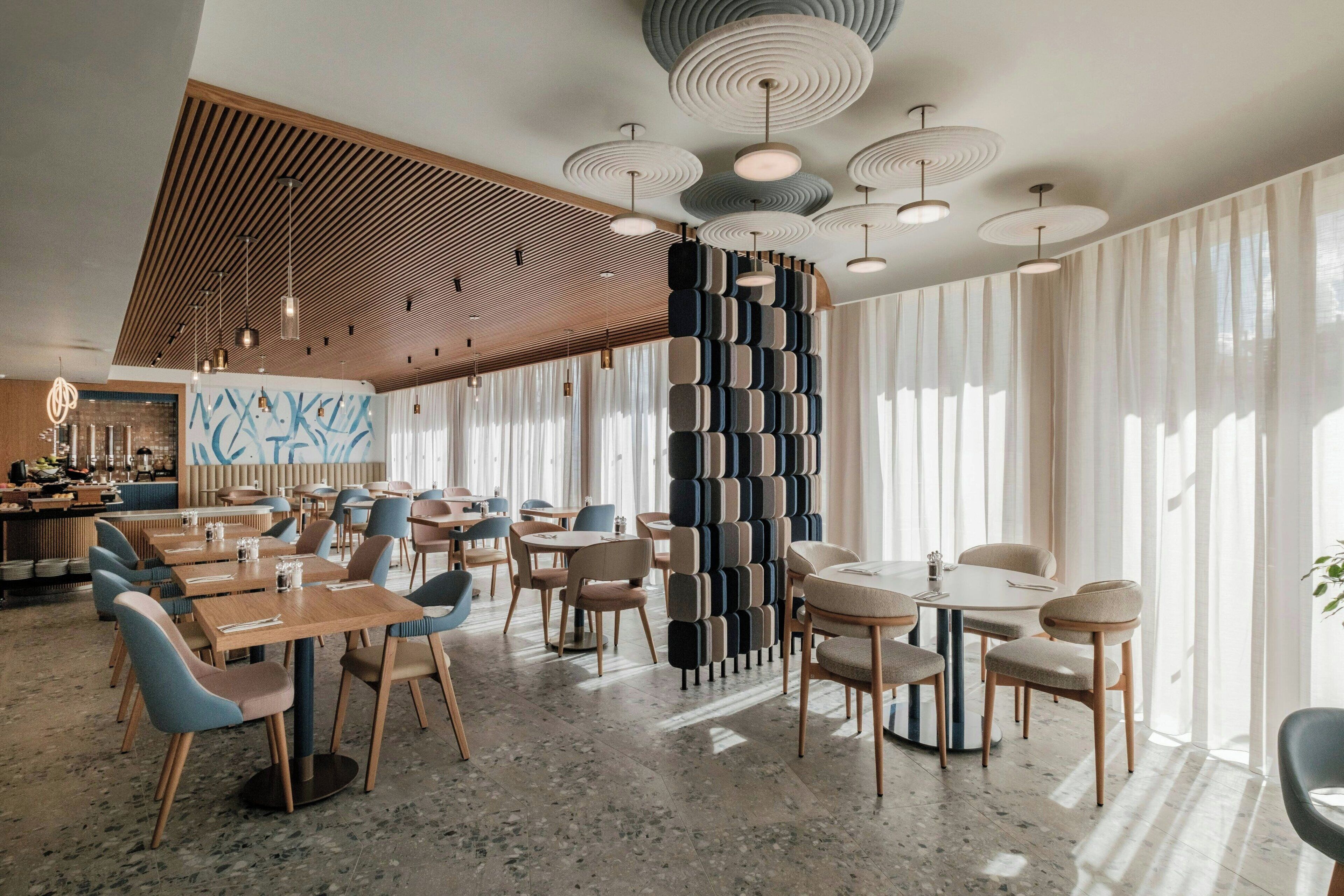 Restaurante moderno com várias áreas de refeição, painéis de teto em madeira e iluminação pendente.