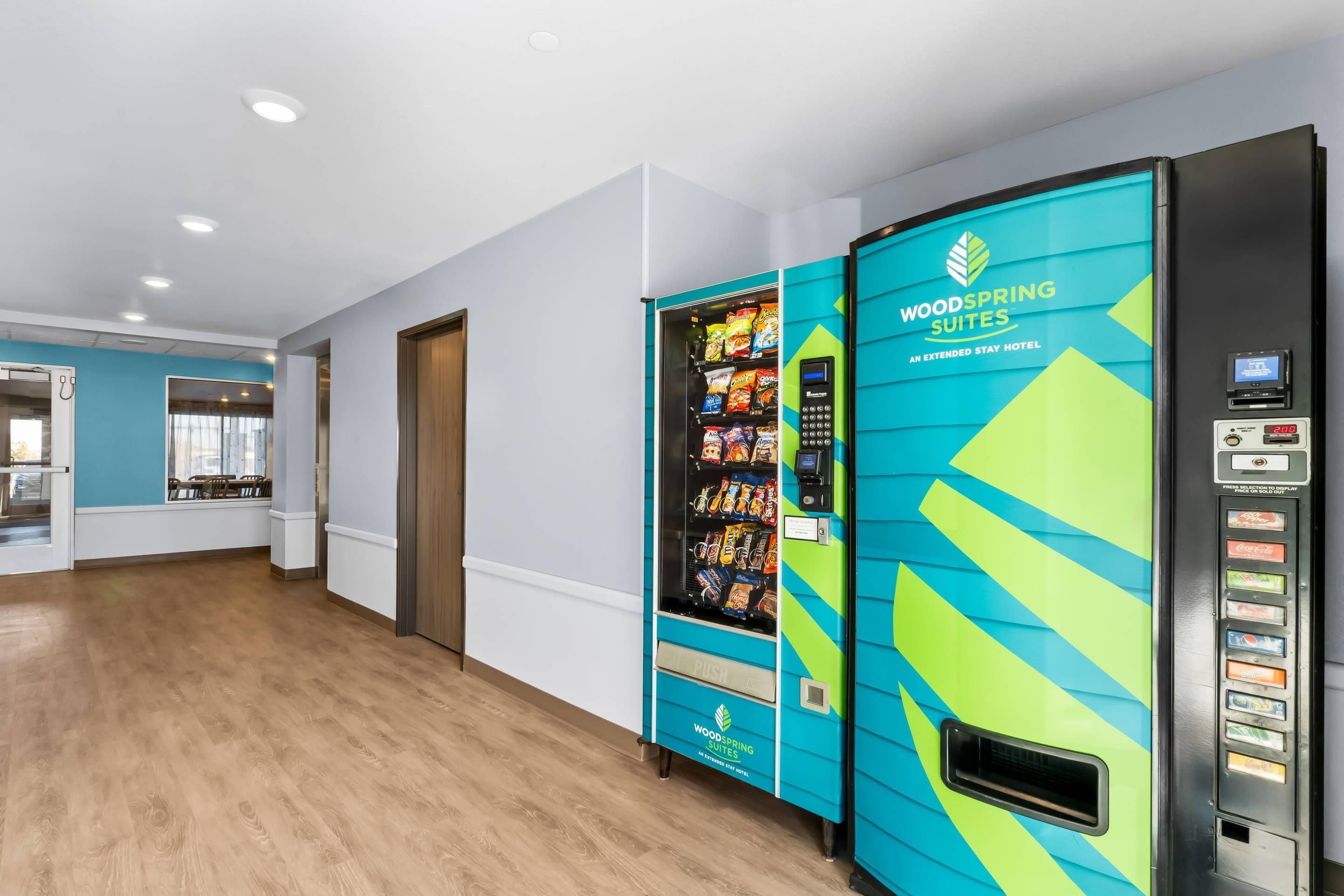 Corredor de hotel com máquina de vendas abastecida com lanches e um painel digital.