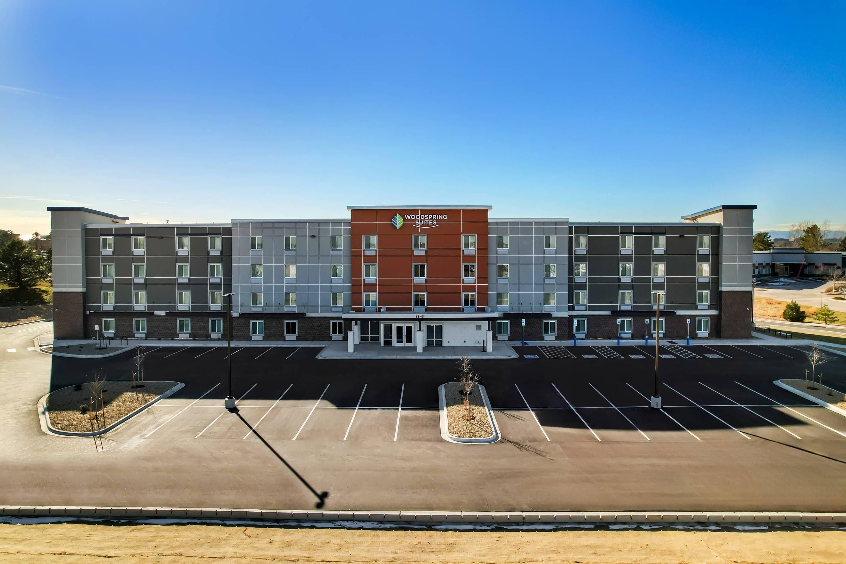 Um hotel de vários andares com entrada central, estacionamento e céu claro.