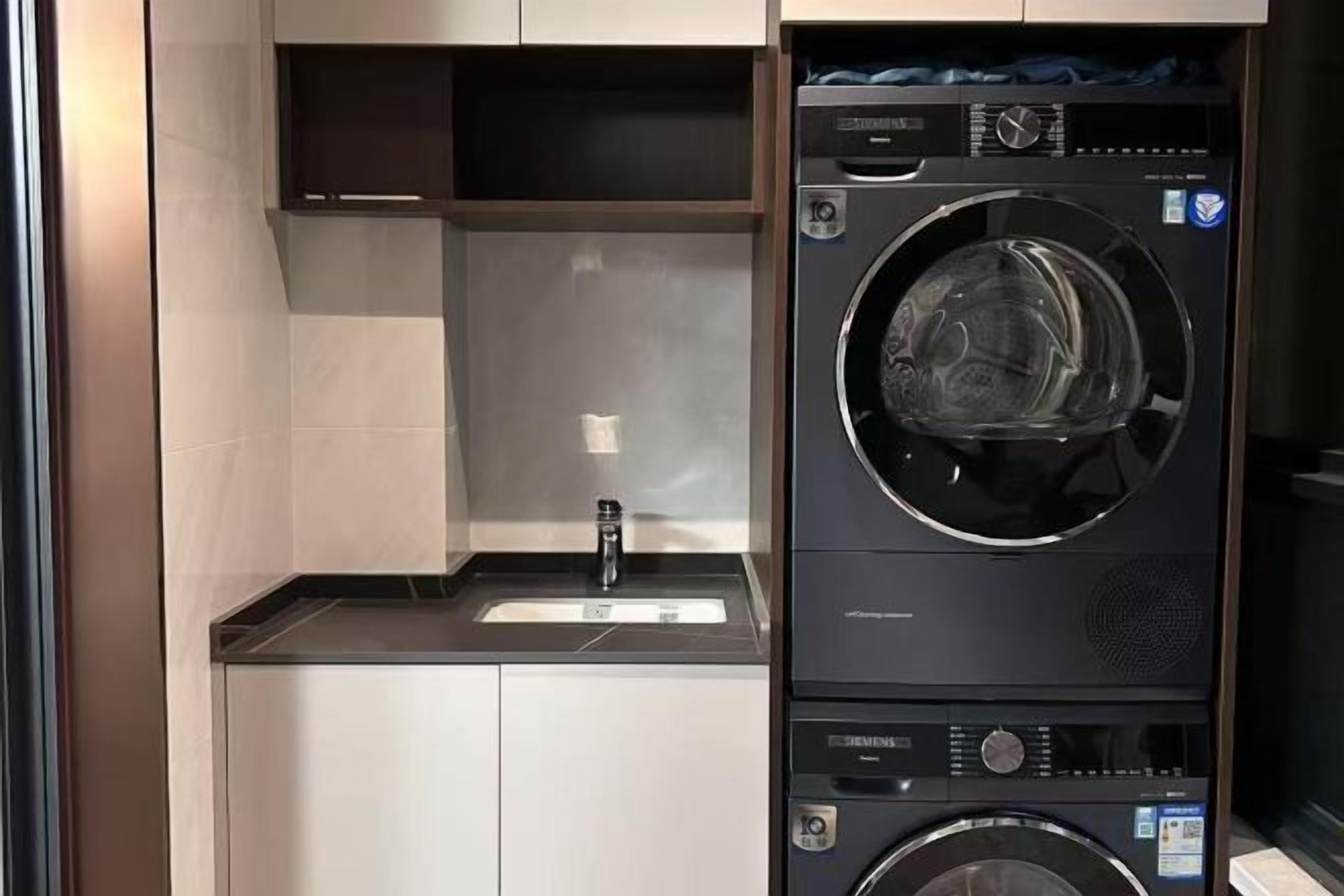 Máquina de lavar e secar compacta com painel de controle, localizada em uma pequena área de cozinha com pia e armários.