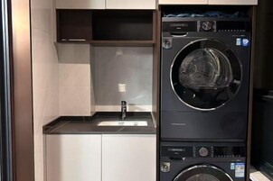 Máquina de lavar e secar compacta com painel de controle, localizada em uma pequena área de cozinha com pia e armários.