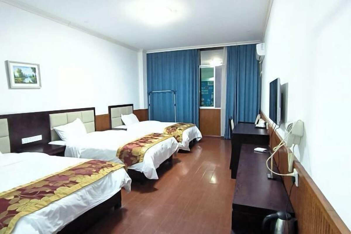 Quarto de hotel com duas camas, uma escrivaninha, uma cadeira, televisão e janela com cortinas.