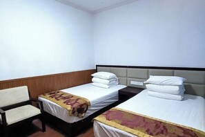 Quarto de hotel com duas camas de solteiro, uma cadeira de madeira e uma mesa pequena.