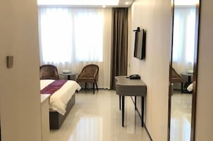 Quarto de hotel com cama, escrivaninha, cadeira e televisão.