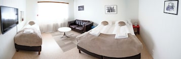 Quarto de hotel com duas camas, um sofá, uma televisão e obras de arte nas paredes.