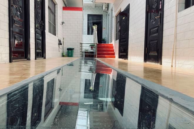 Um corredor com piso refletivo, portas pretas e degraus vermelhos que levam a um andar superior.