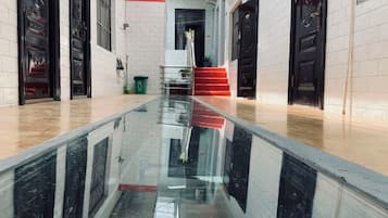 Um corredor com piso refletivo, portas pretas e degraus vermelhos que levam a um andar superior.