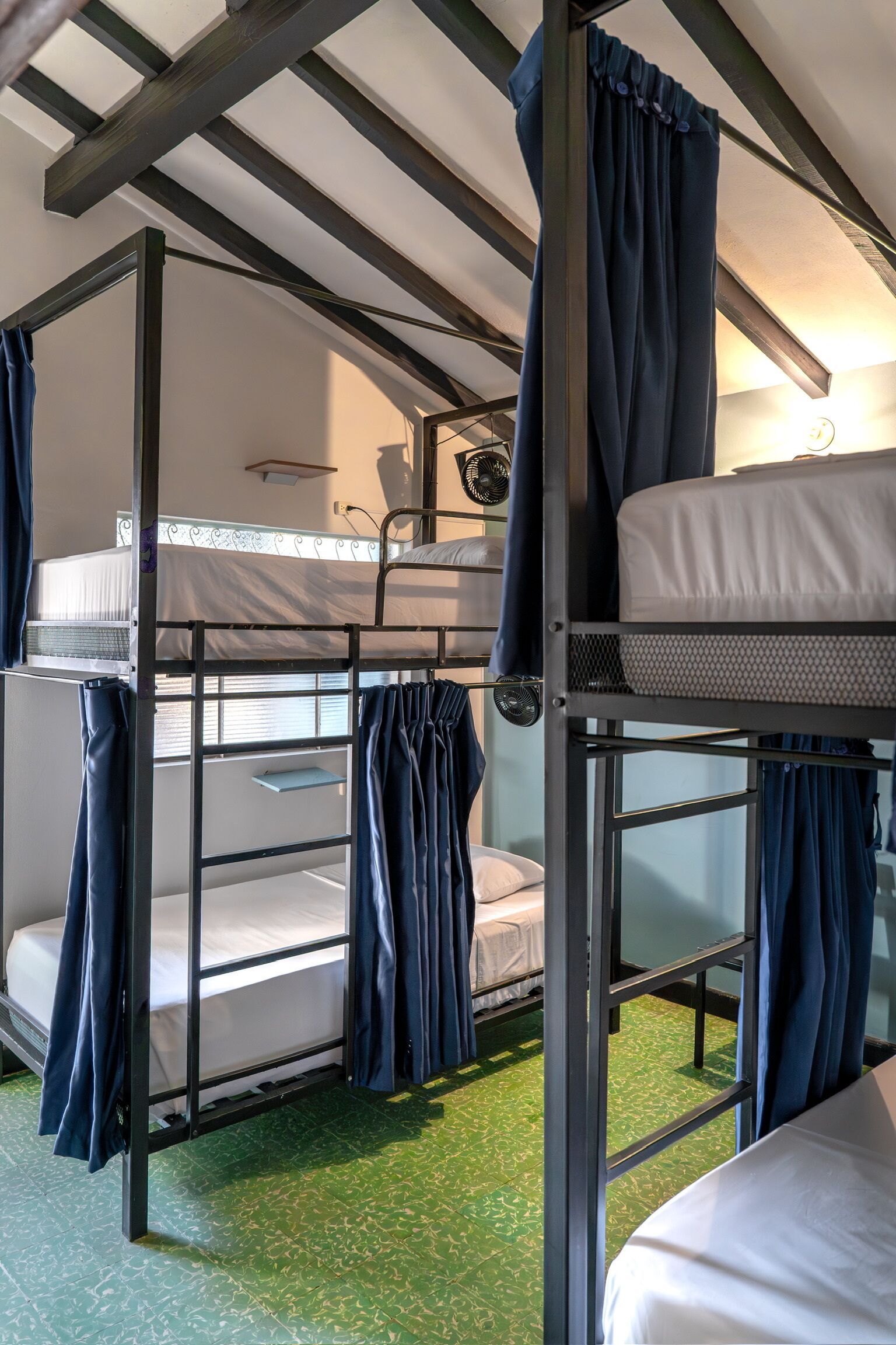 Quarto com beliche, chão com padrão verde, beliches de metal e cortinas azuis.