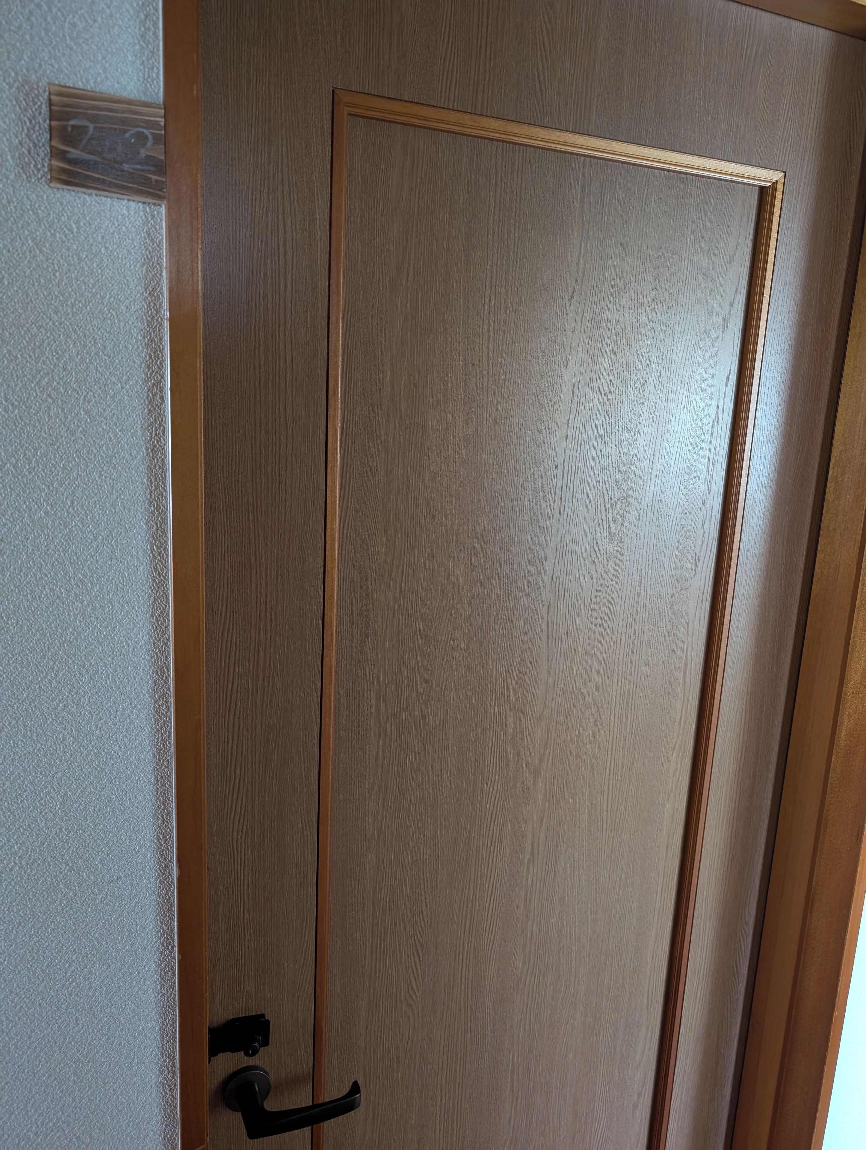 Uma porta de madeira com design simples e uma pequena placa na parede à esquerda.