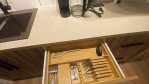 Uma gaveta de cozinha com utensílios e um objeto preto na bancada.